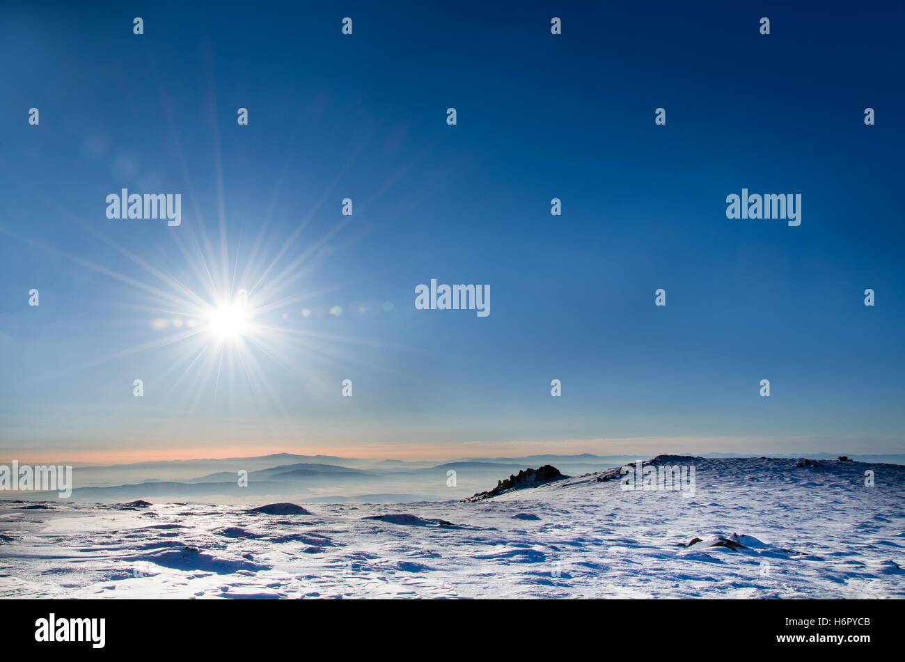 Winter landscape with a raising sun and sun rays against a clear blue ...