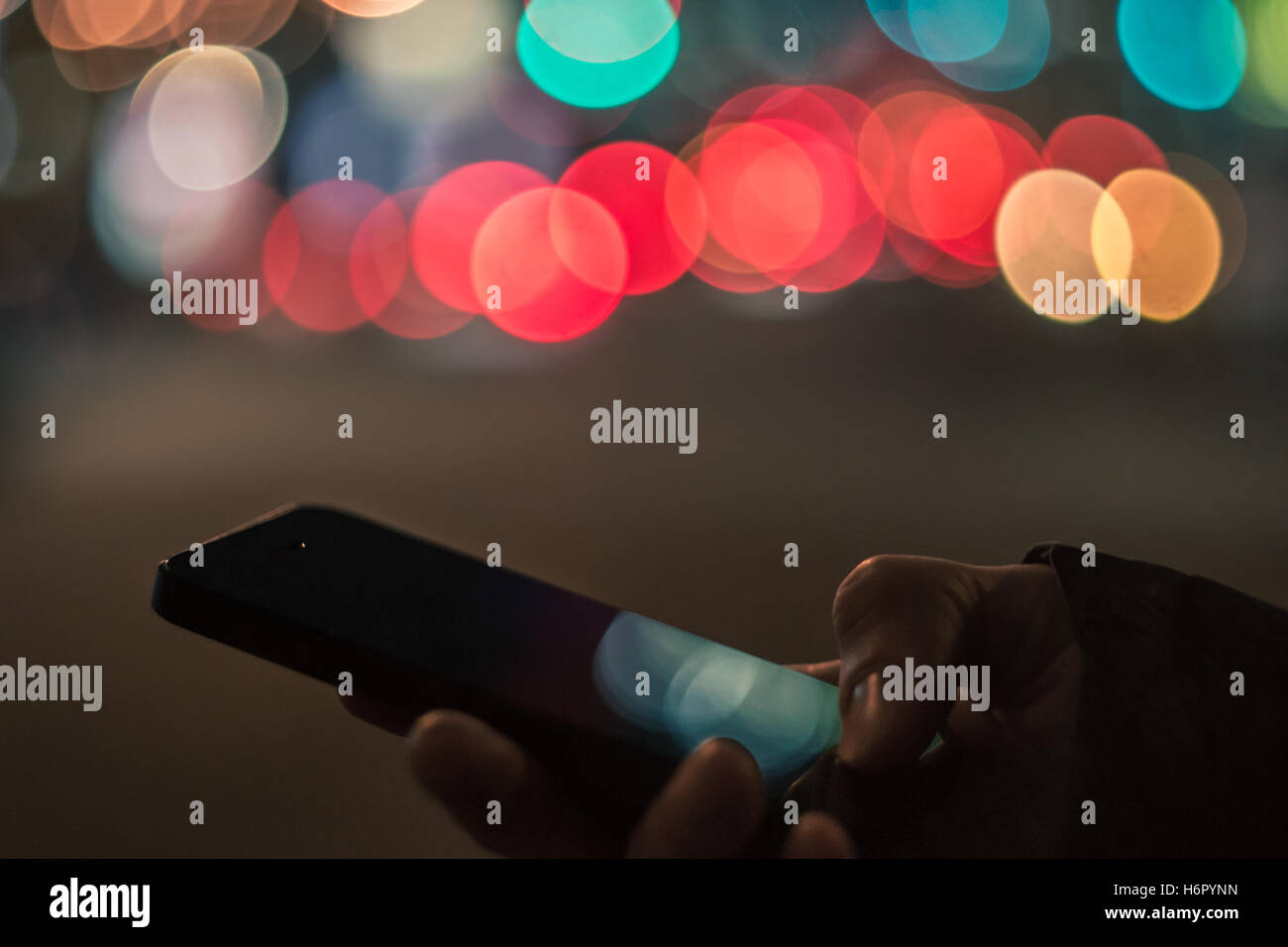 Smart phone in male hands in front of blurred city lights bokeh. Man ...