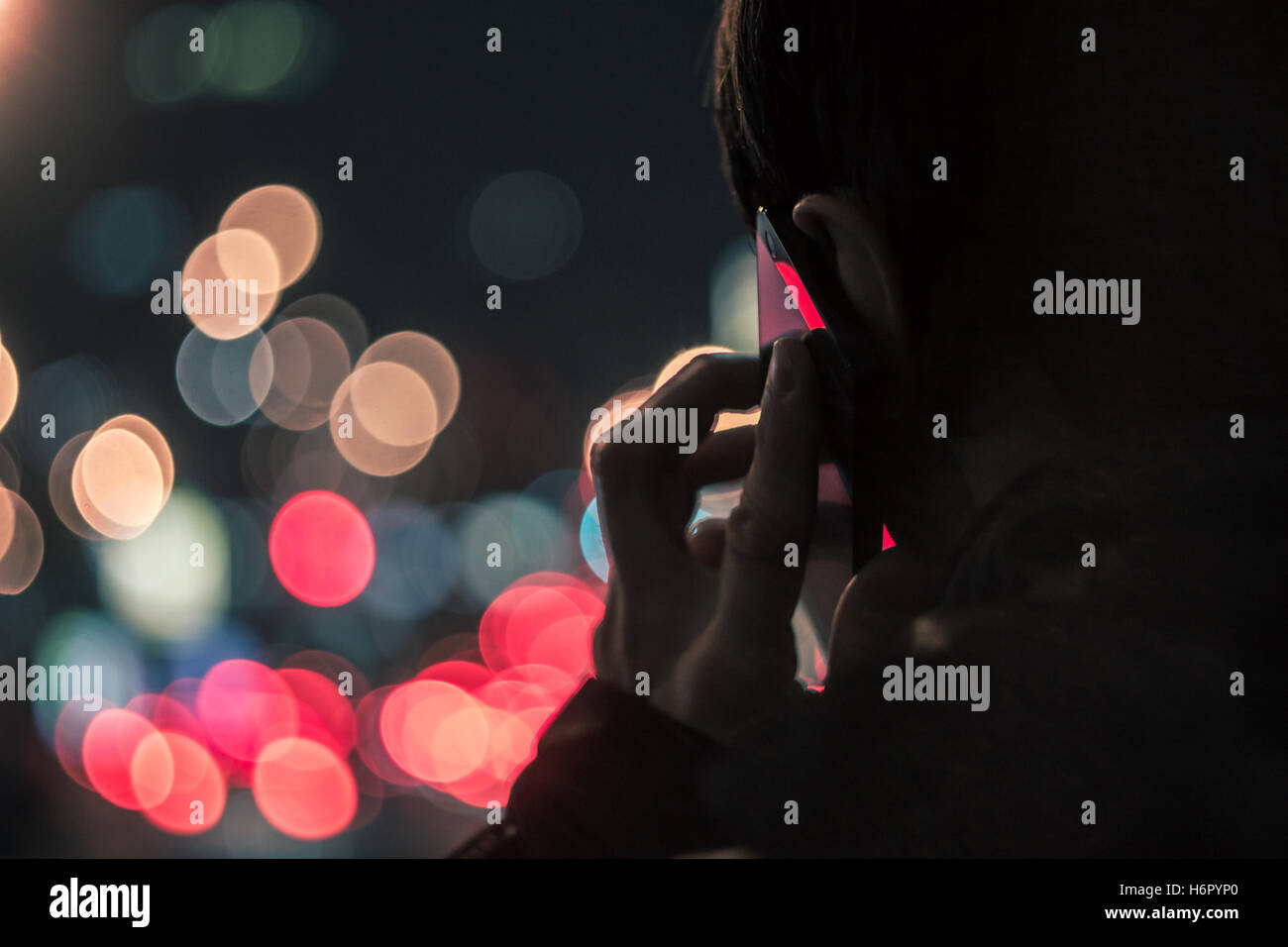 Young man talking on mobile phone at night in front of blurred city ...