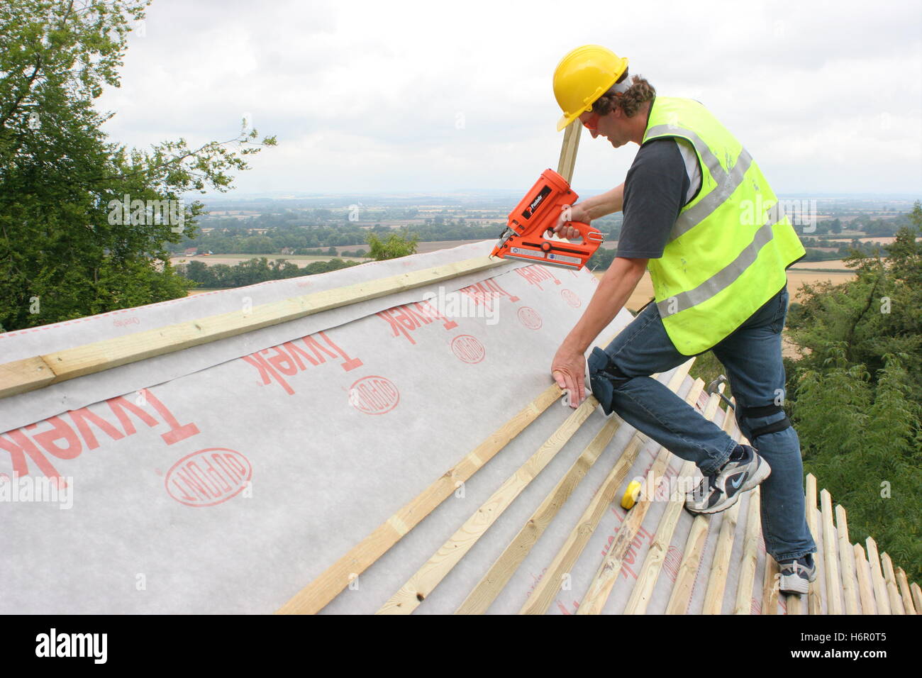 A Single Roofer Nails Timber Battens To The Roof Of A Timber House On An Oxfordshire Hillside
