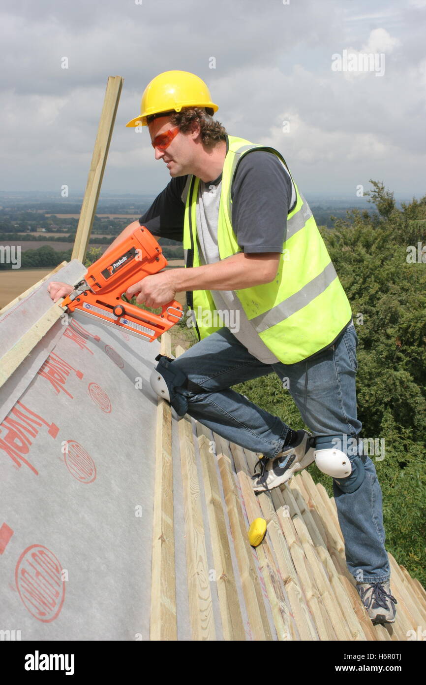 A single roofer nails timber battens to the roof of a timber house on ...