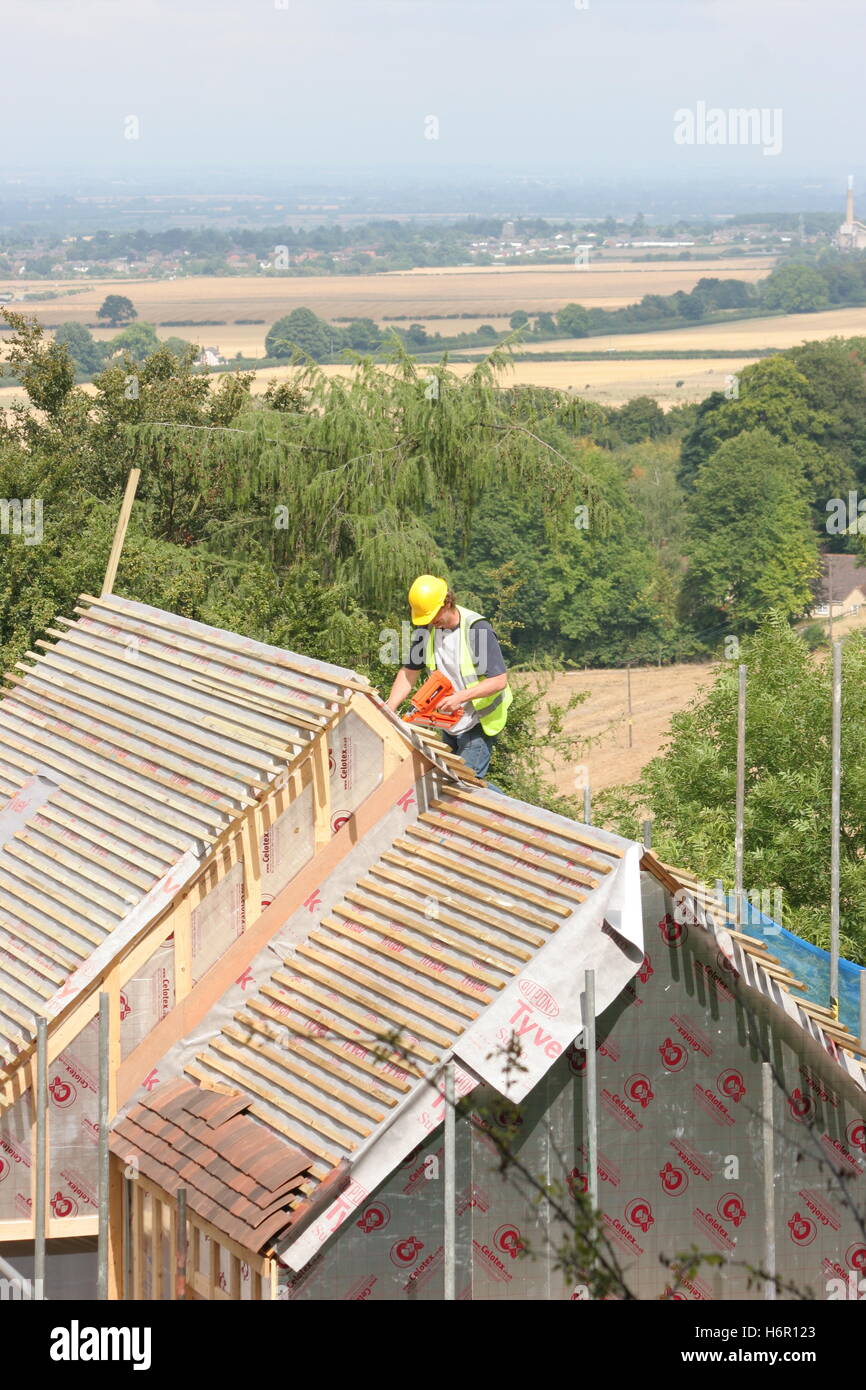 A single roofer nails timber battens to the roof of a timber house on ...