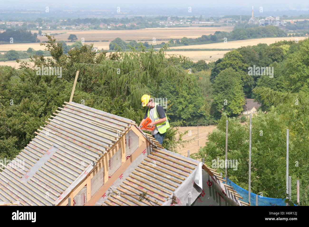 A single roofer nails timber battens to the roof of a timber house on ...