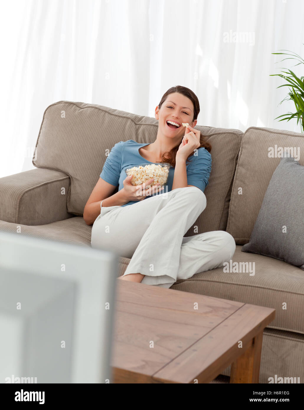 Cheerful woman watching television and eating pop corn in the living ...
