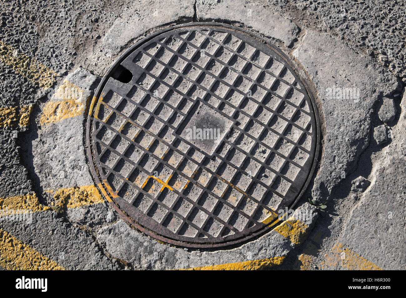 Round metal hatch in urban pavement, sewer manhole cover with yellow ...