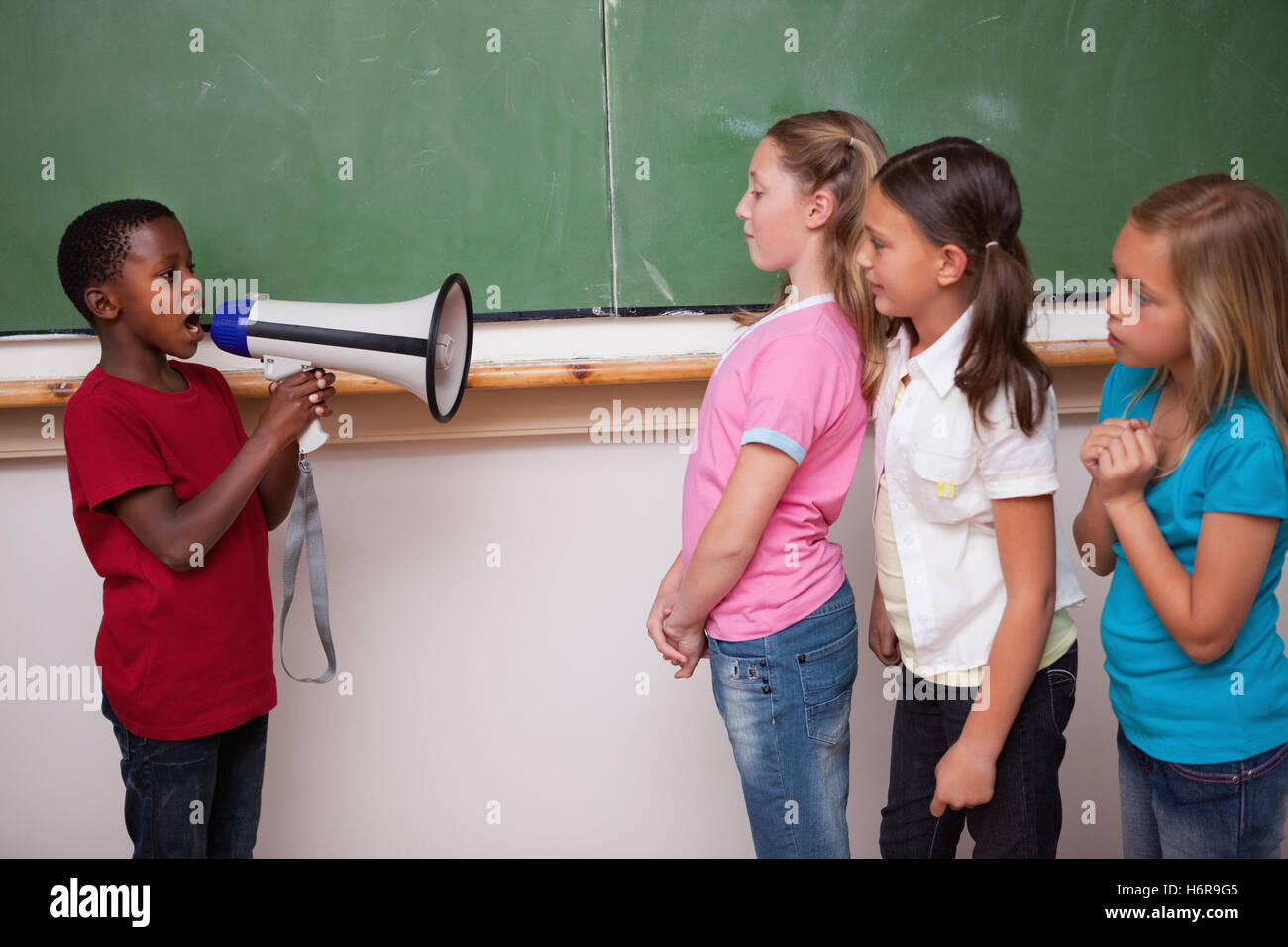 Schoolboy yelling through a megaphone to his classmates in a classroom ...