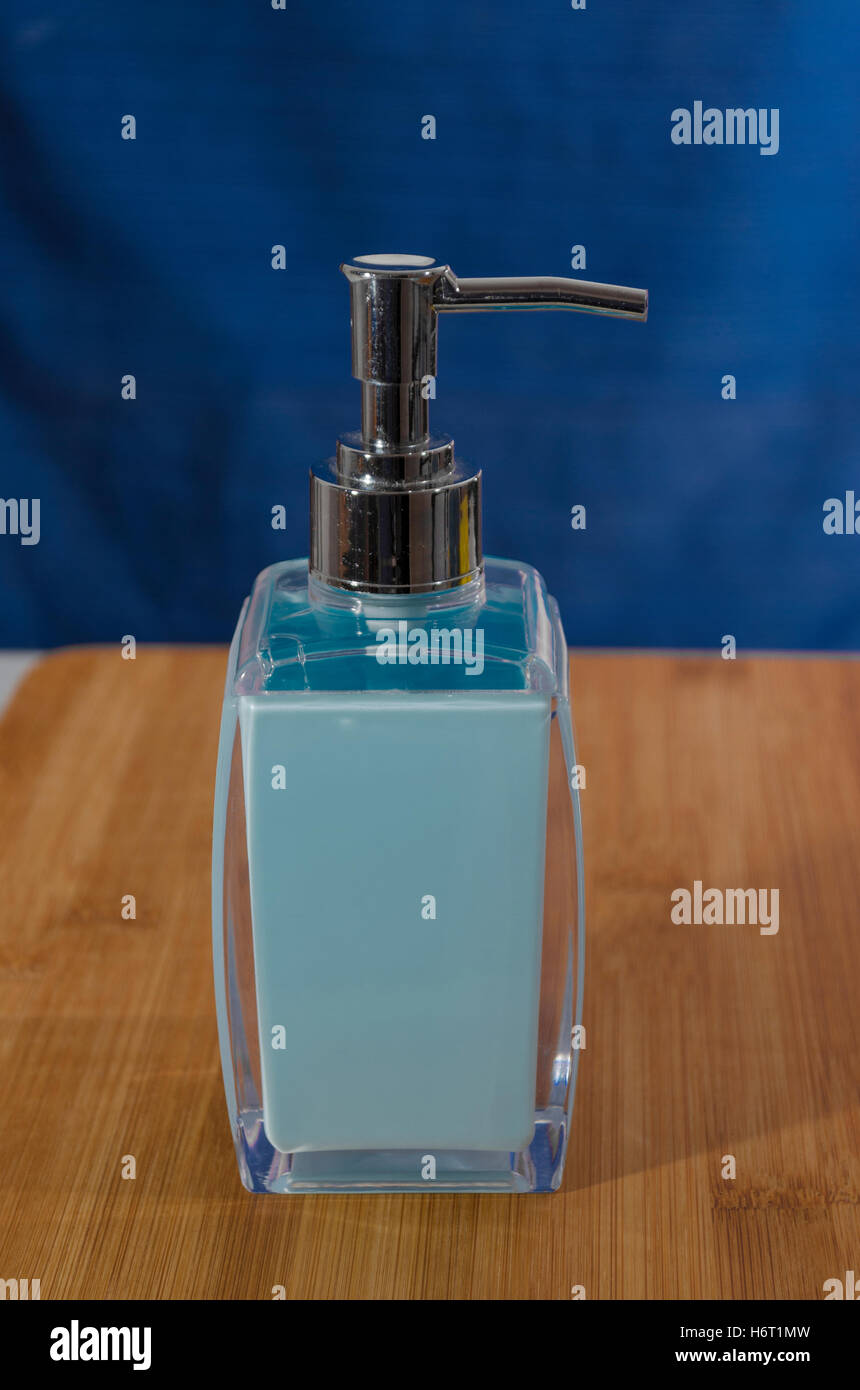 Light blue liquid soap dispenser with a chrome top on a wooden shelf ...
