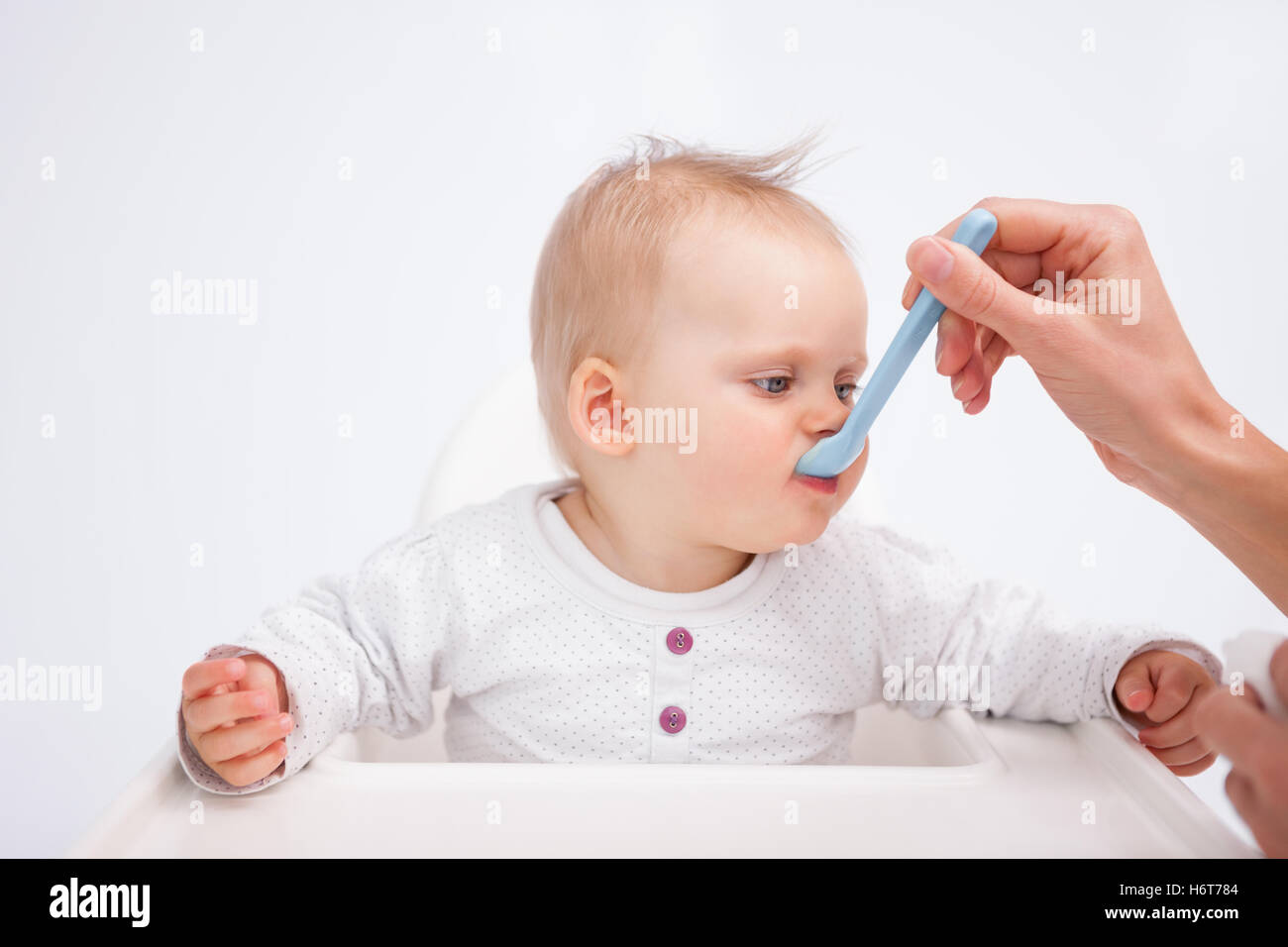 Cute baby eating while being accompanied by her mother against a grey ...