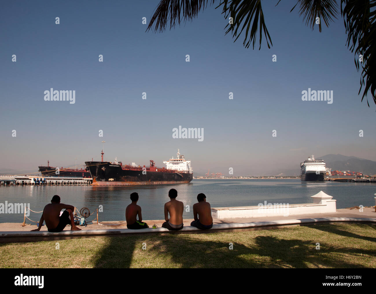 Young Men sitting on the dock side in the shade, watching ships coming ...