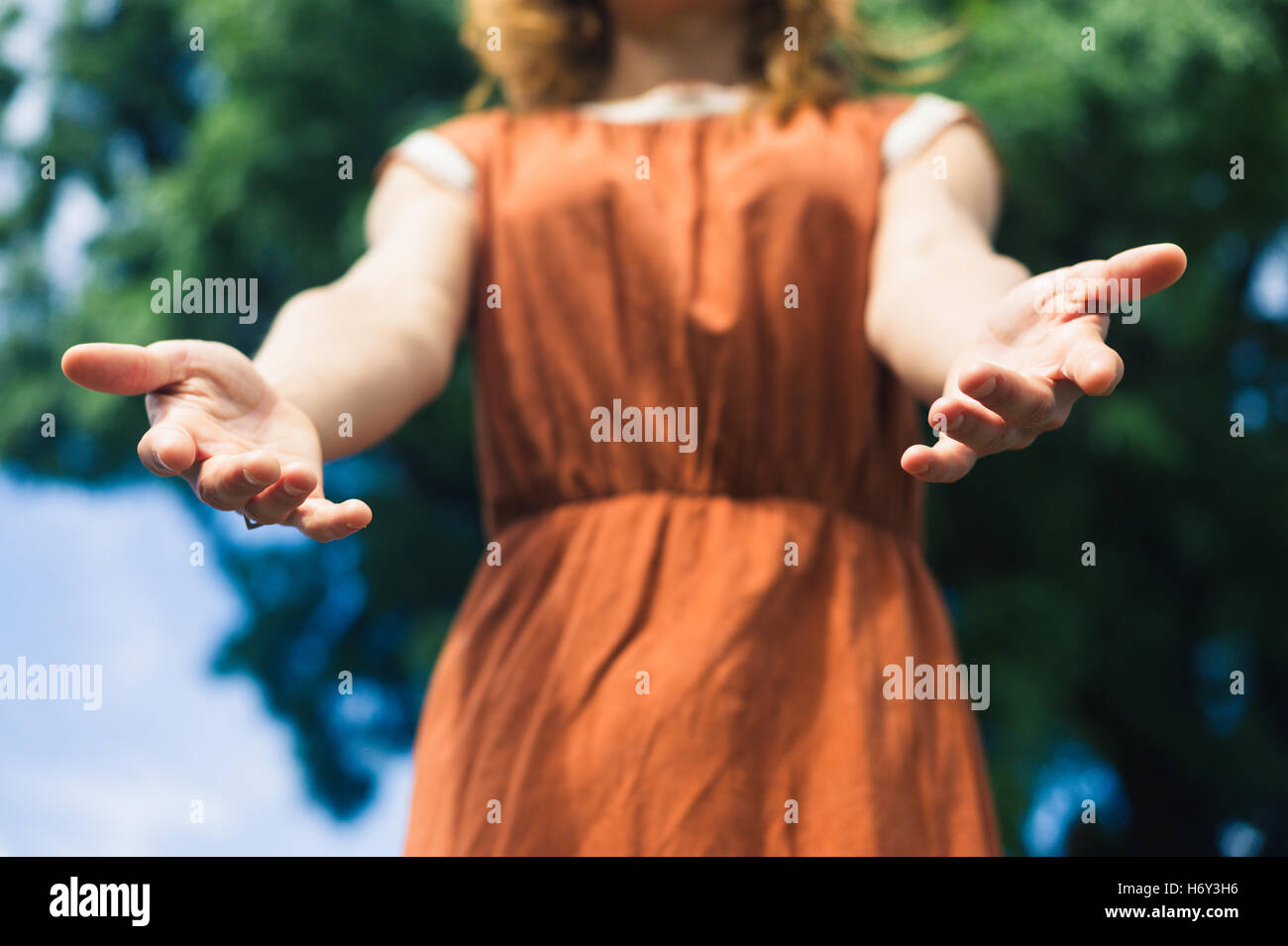 A young woman is standing in nature and is offering her hands to help ...