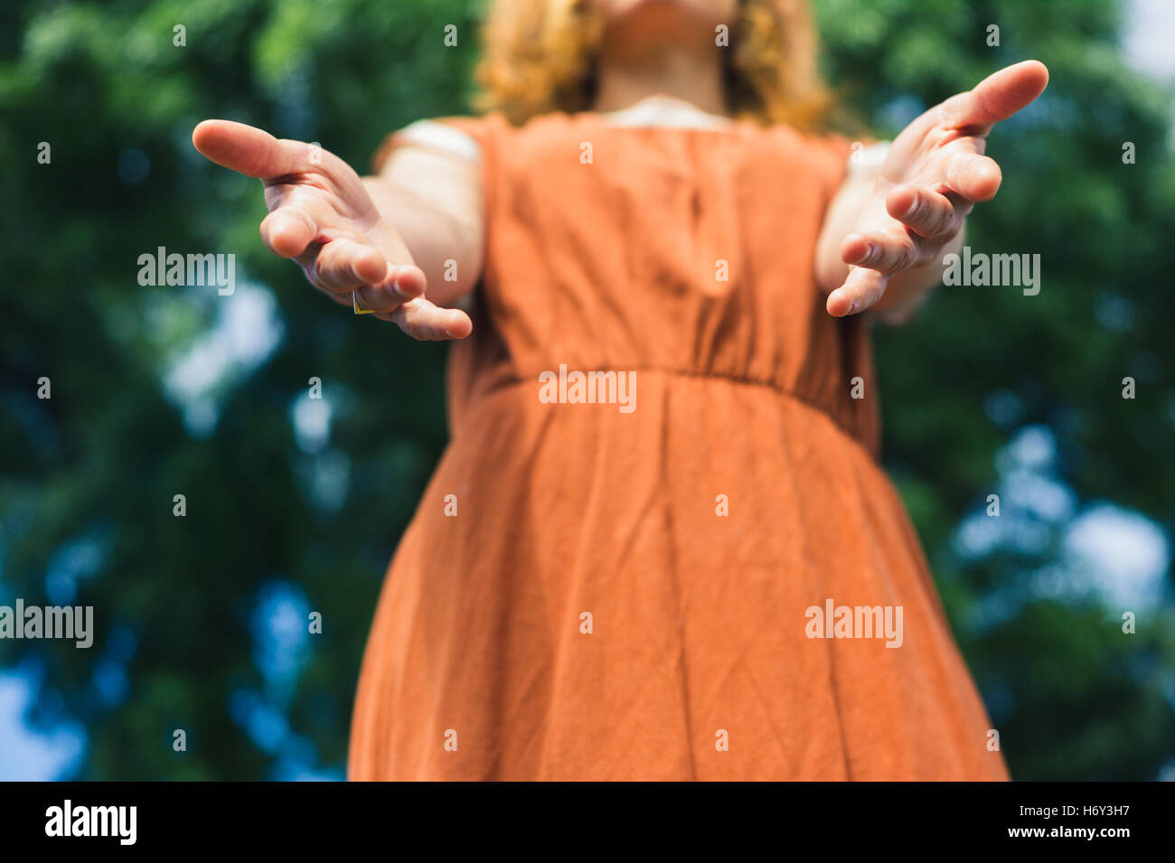 A young woman is standing in nature and is offering her hands to help ...