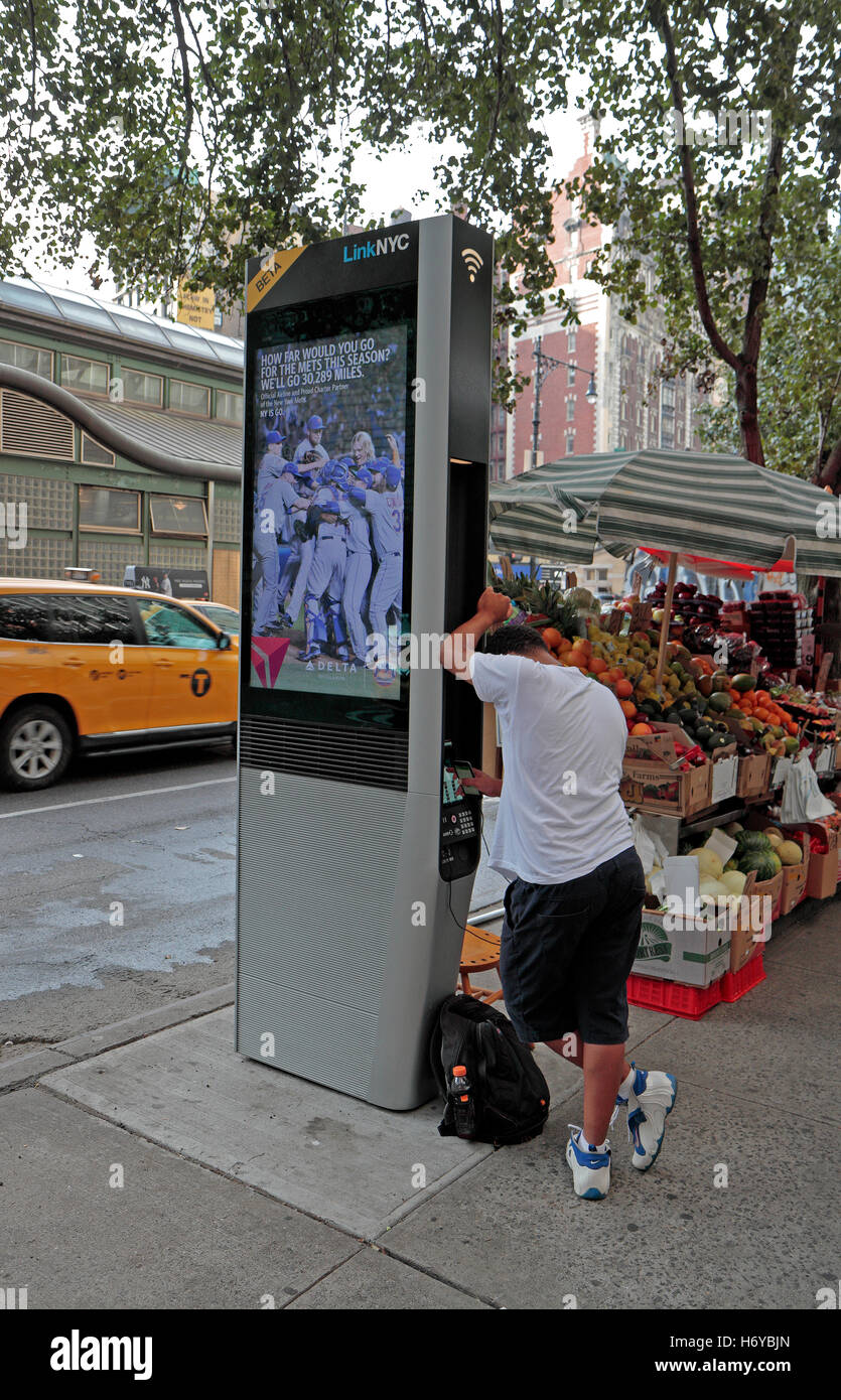 A man using a LinkNYC kiosk to charge his phone in Manhattan, New York ...