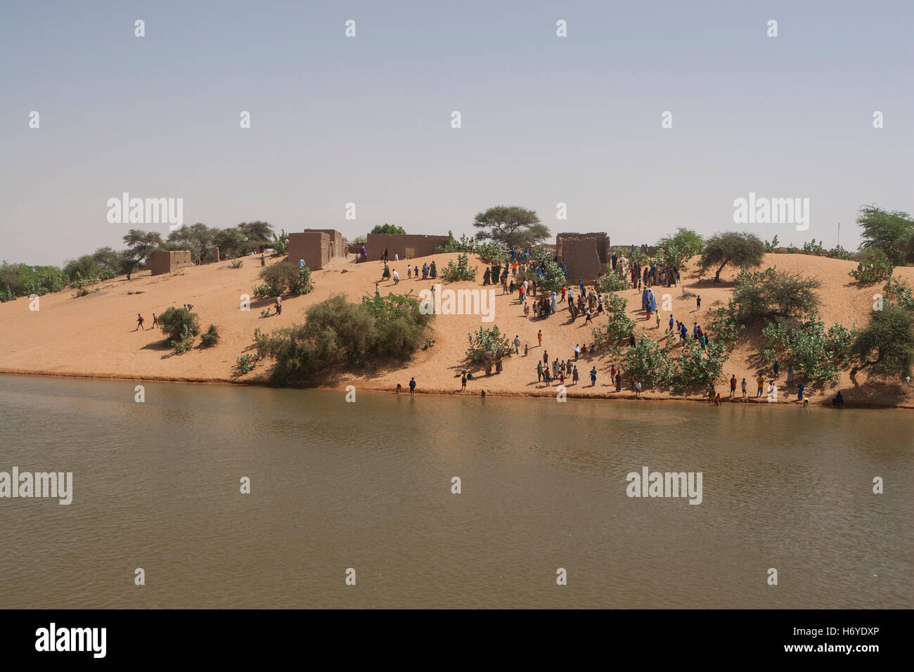 People gathering on the banks of River Niger near a traditional adobe ...
