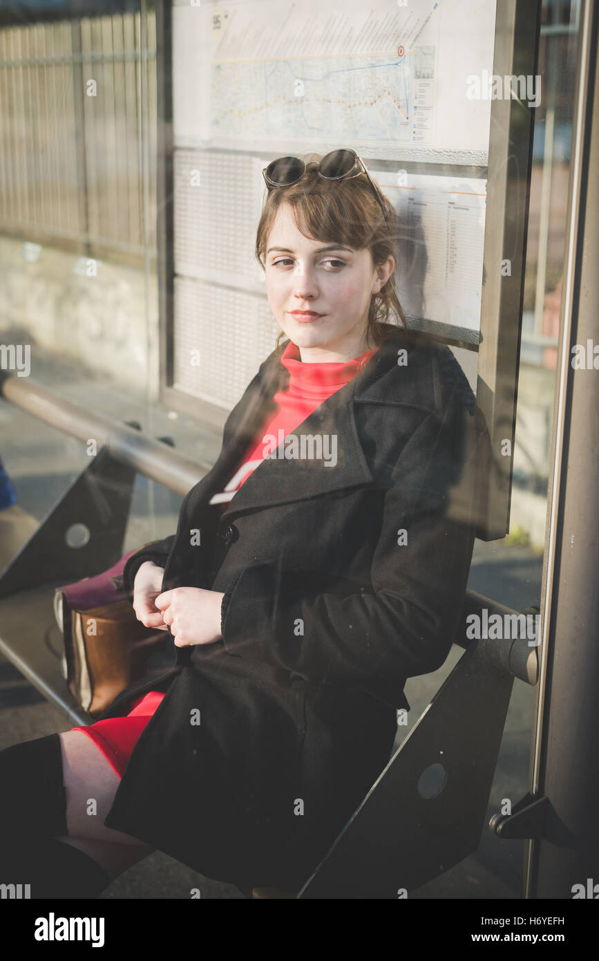 Young beautiful vintage caucasian woman sitting at bus stop - commuter ...
