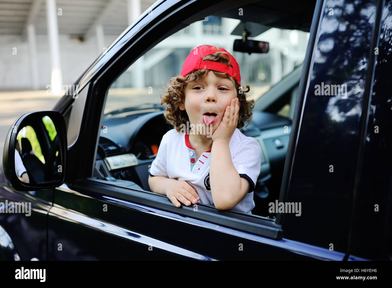 child with curly hair and a red cap sits behind the wheel of car Stock ...