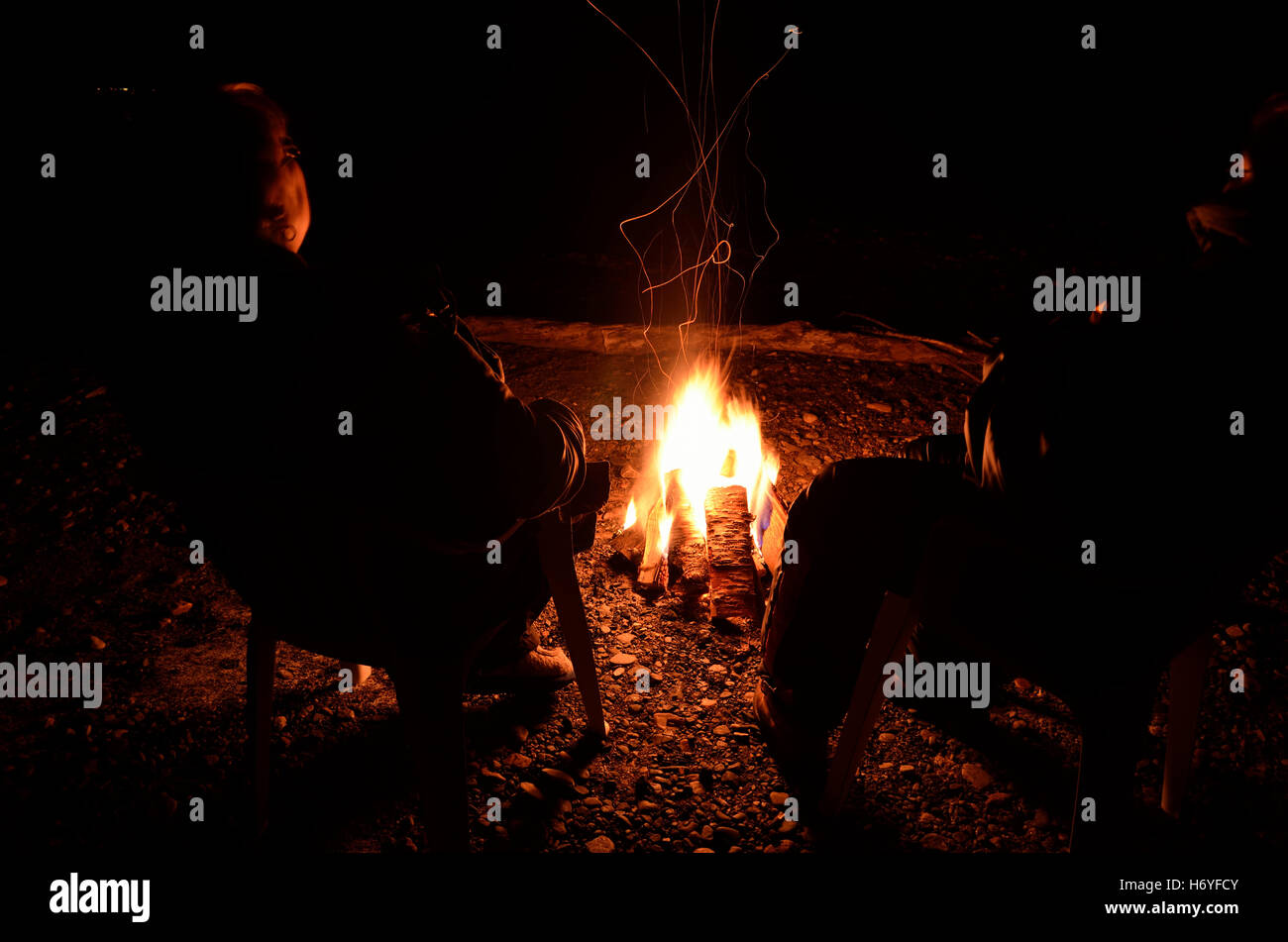 two people sitting around warming campfire in cold autumn wilderness in ...