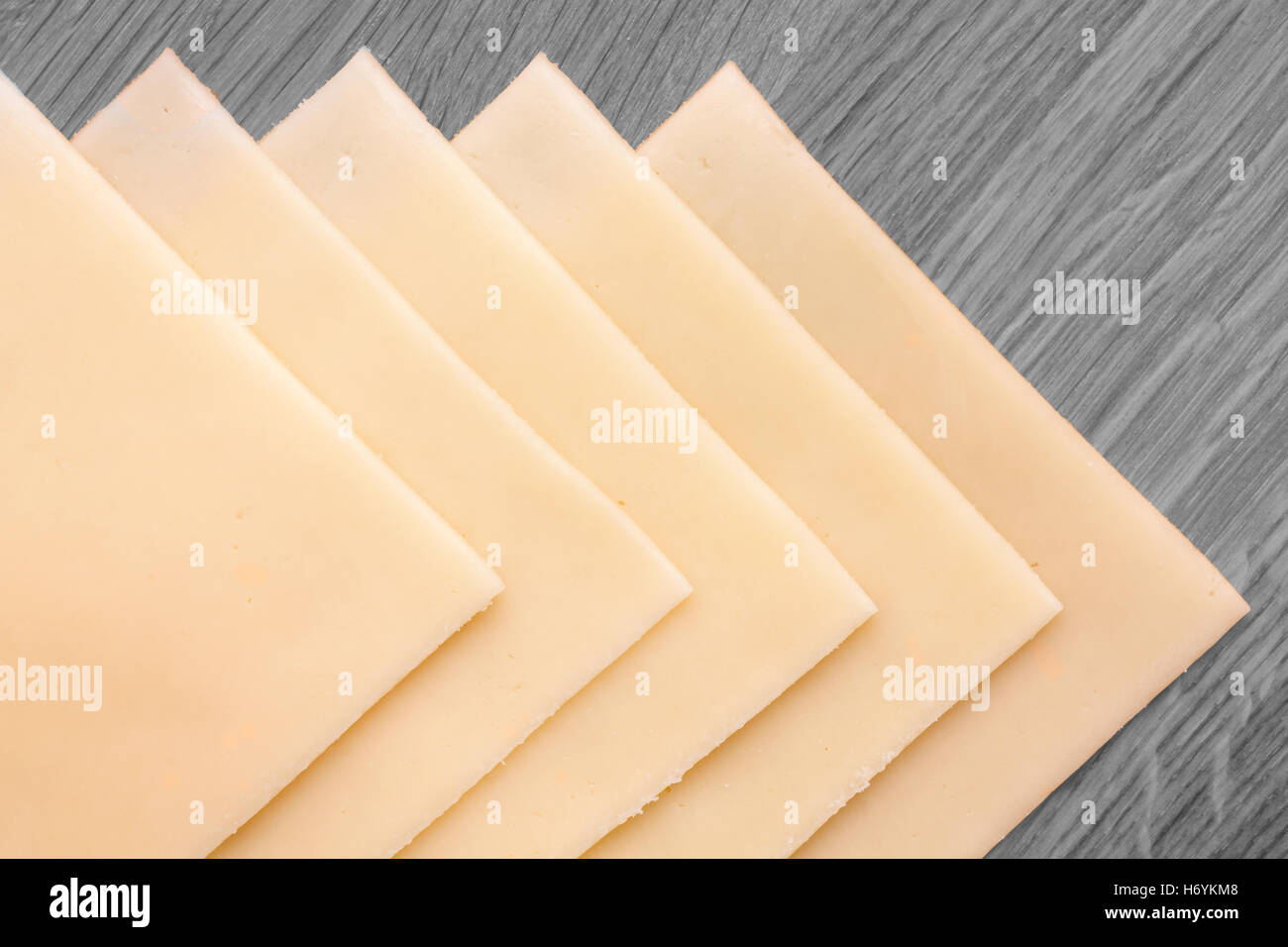 Sliced yellow sandwhich cheese neatly arranged on a wood surface. Shot ...