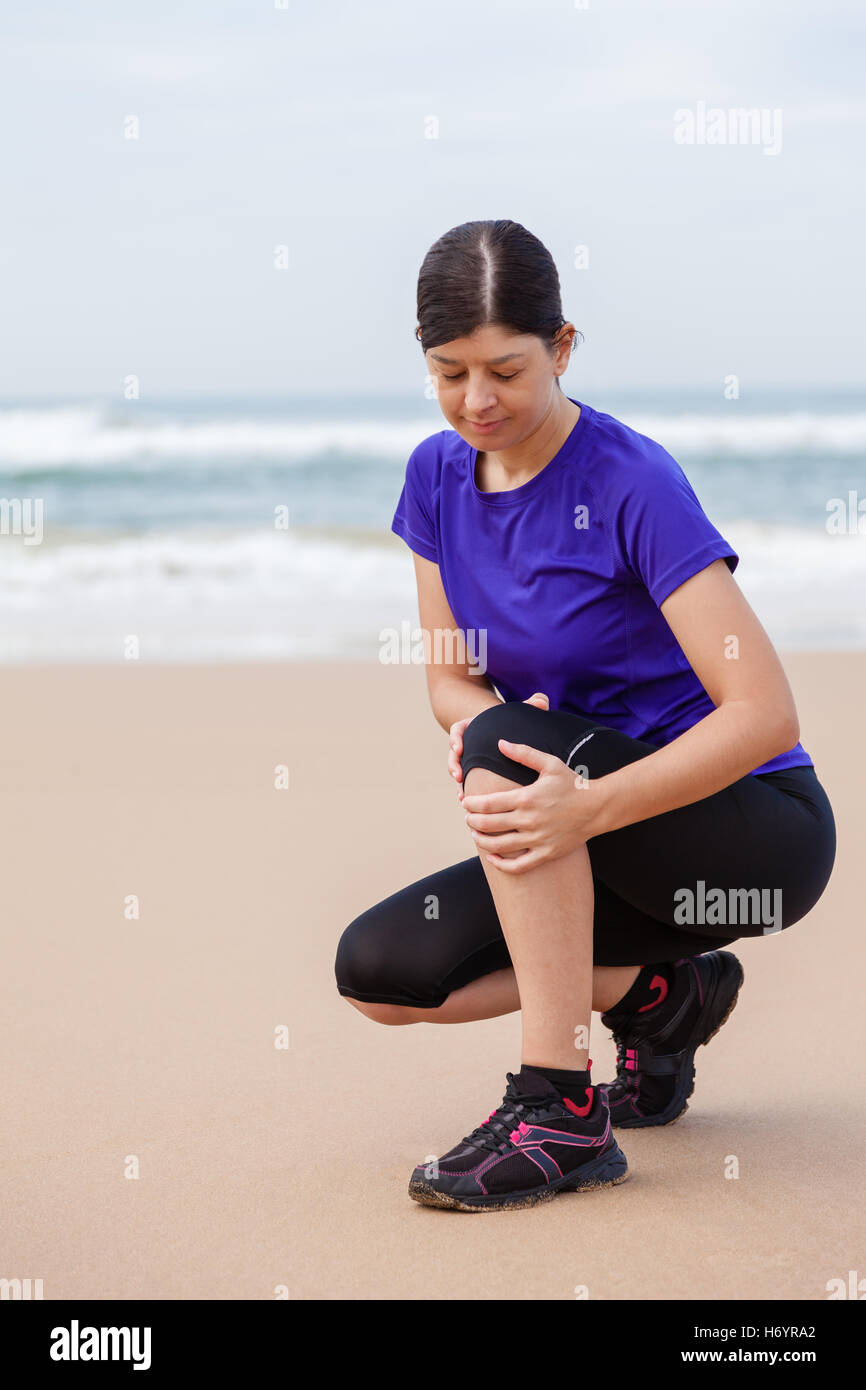 Female athlete suffering from a knee injury at the beach on an Autumn ...