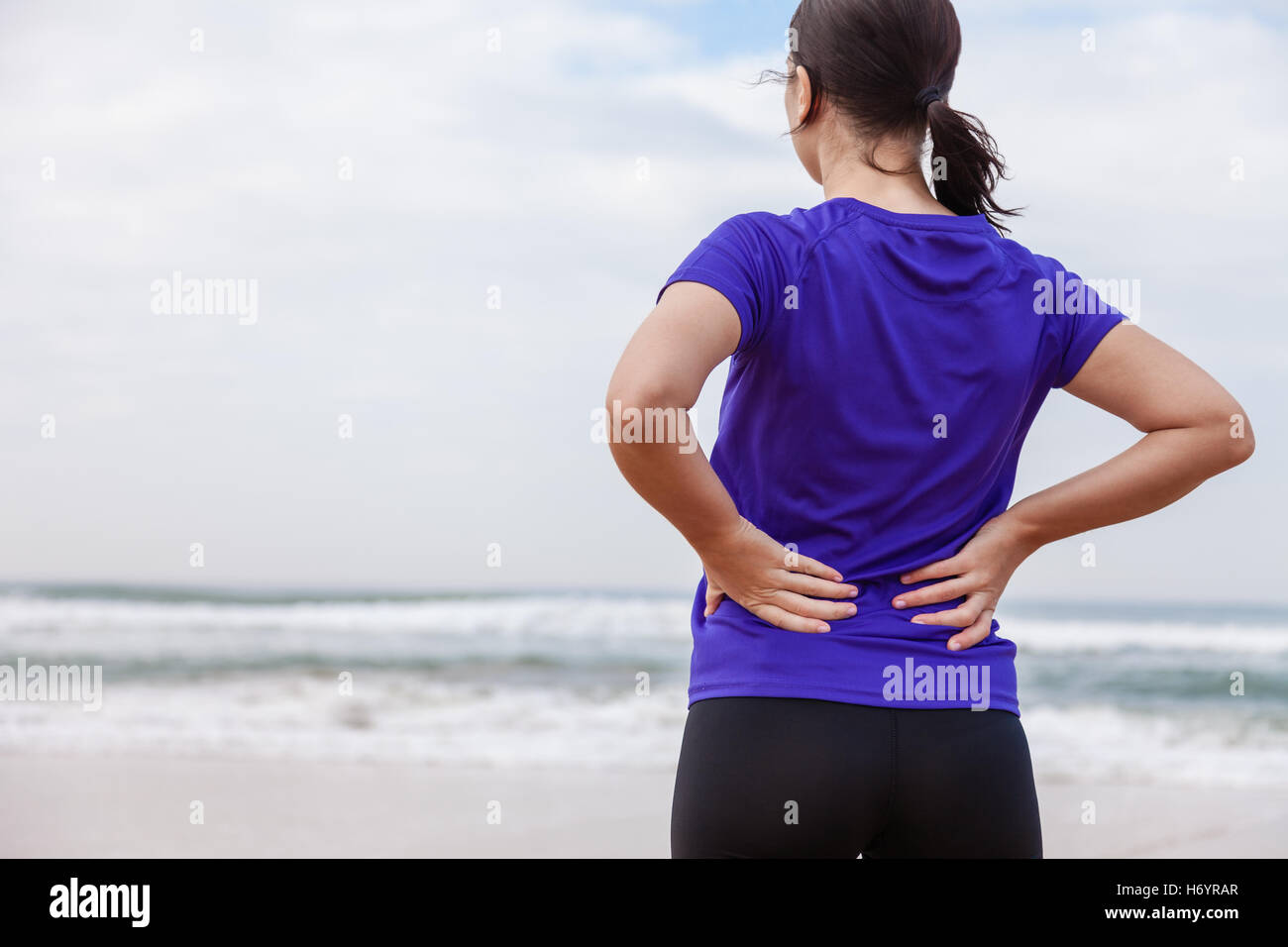 Female athlete suffering from a back injury at the beach on an Autumn ...