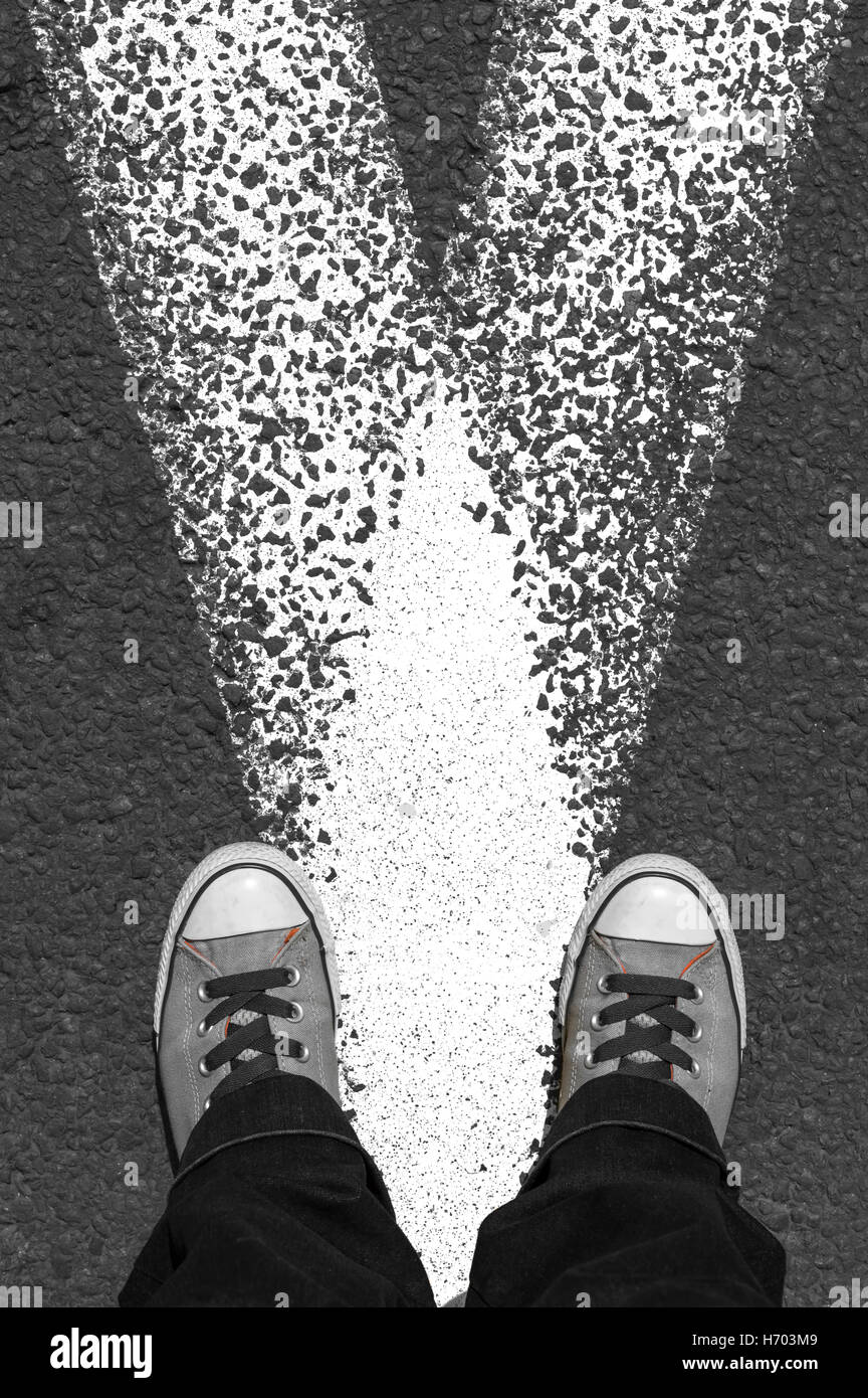 Sneakers stand on asphalt pavement with the white road marking lines ...