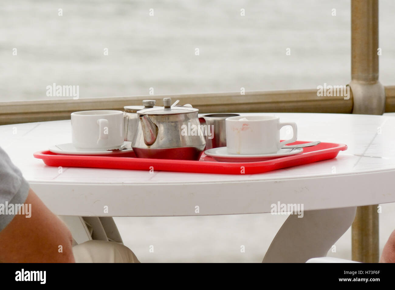 Teapot and cups on red plastic tray on table at seaside cafe Stock ...