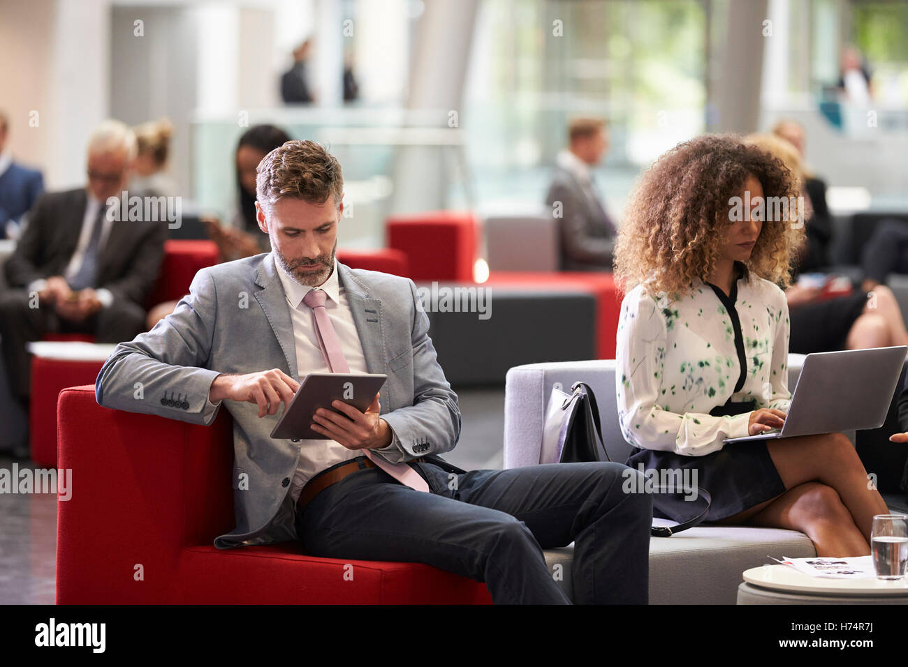 Businesspeople Using Digital Devices In Busy Office Lobby Stock Photo ...