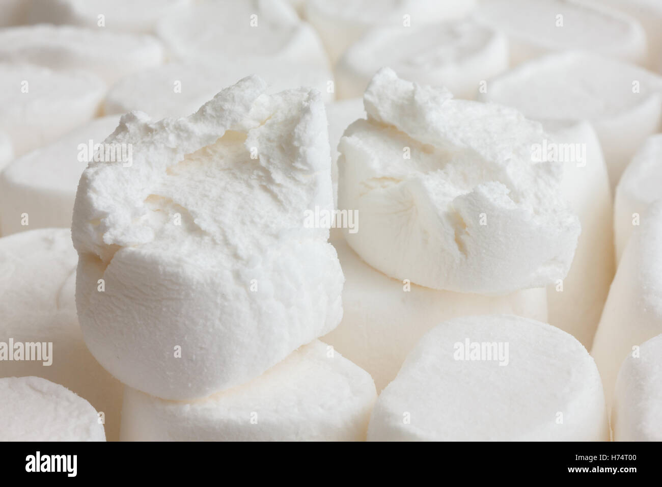 Single white marshmallow torn in two sitting on other marshmallows ...