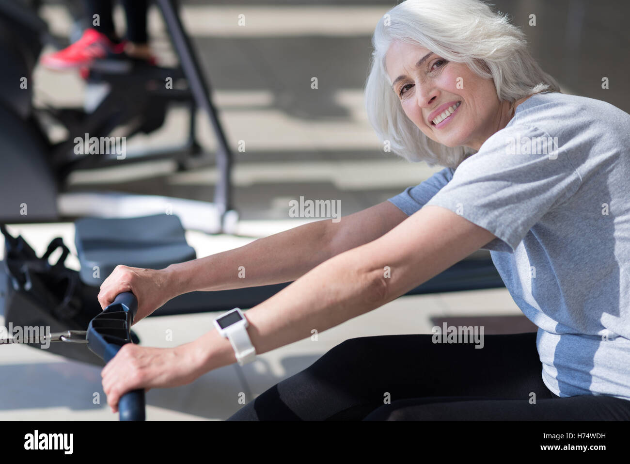 Smiling pretty woman using rowing machine Stock Photo - Alamy