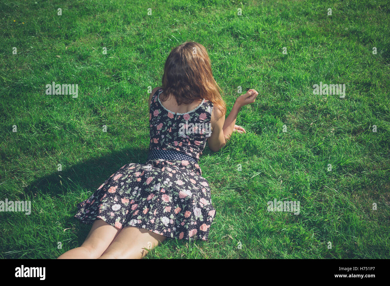 A young woman wearing a dress is lying in the green grass on a sunny ...