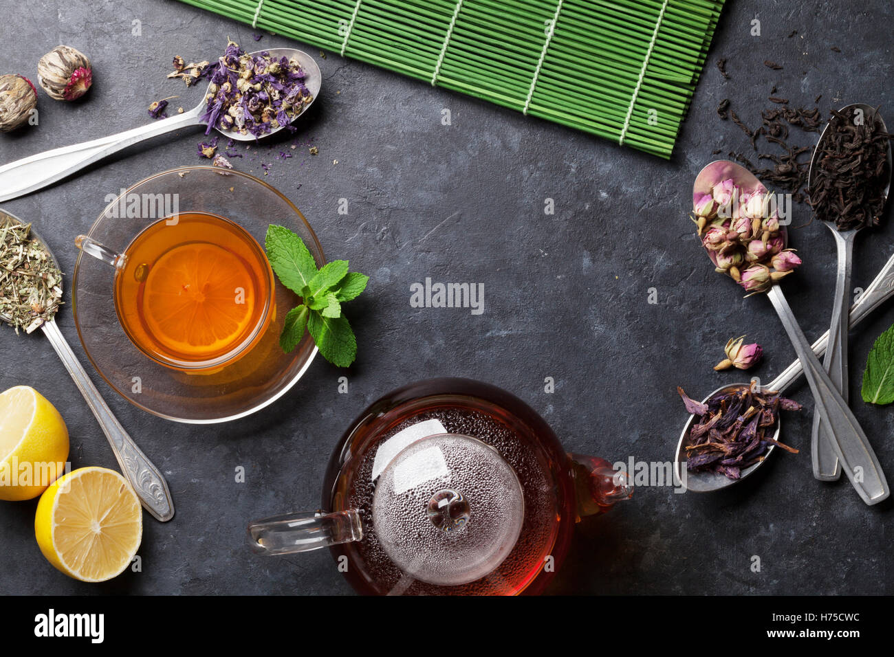 Tea cup, teapot and assortment of dry tea in spoons on stone table. Top ...