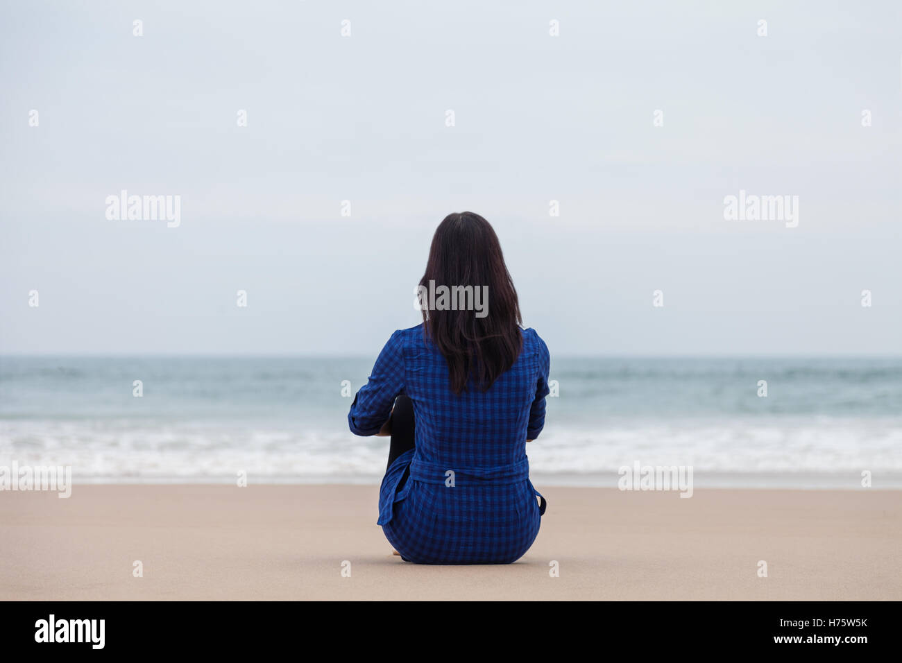 Lonely and depressed woman sitting on the sand of a deserted beach and ...