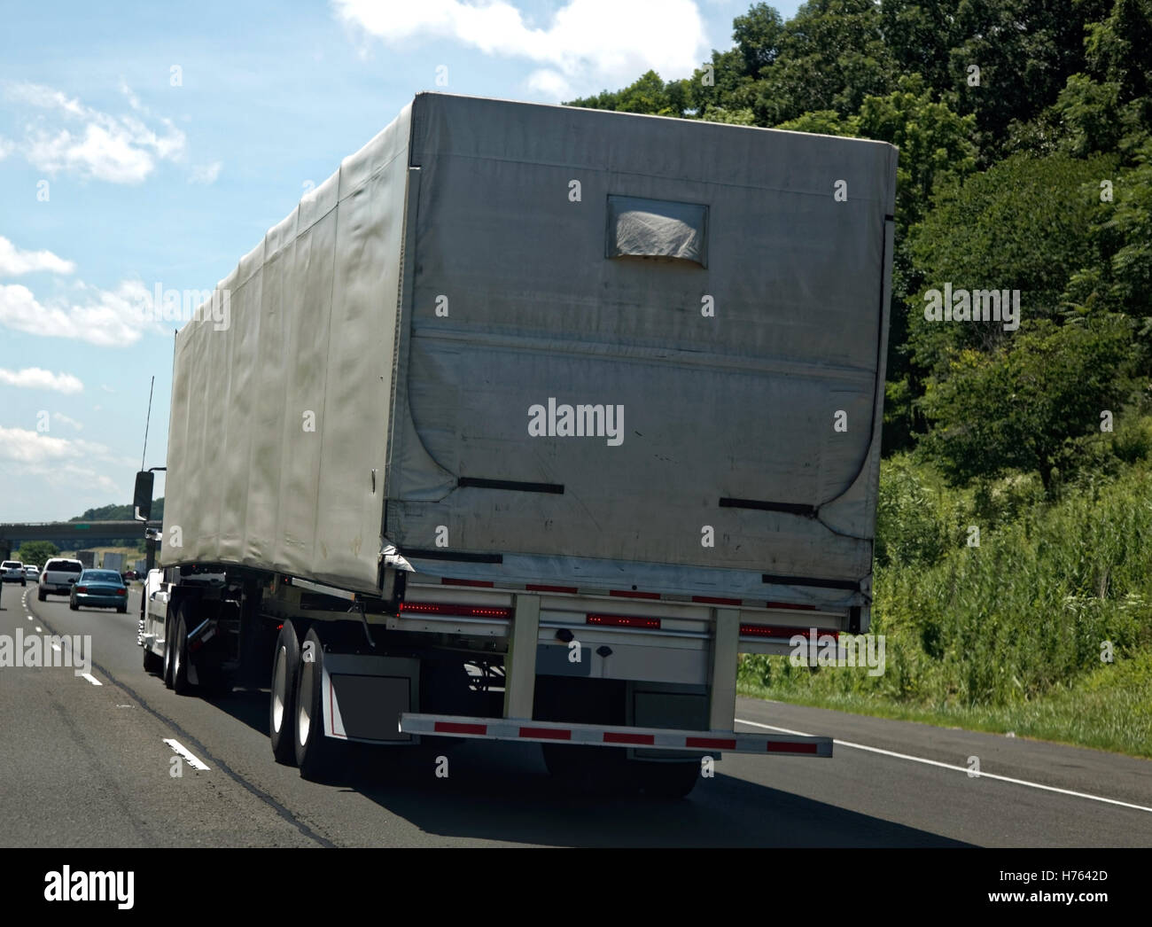 Rear view of covered semi truck and trailer on highway under blue sky ...