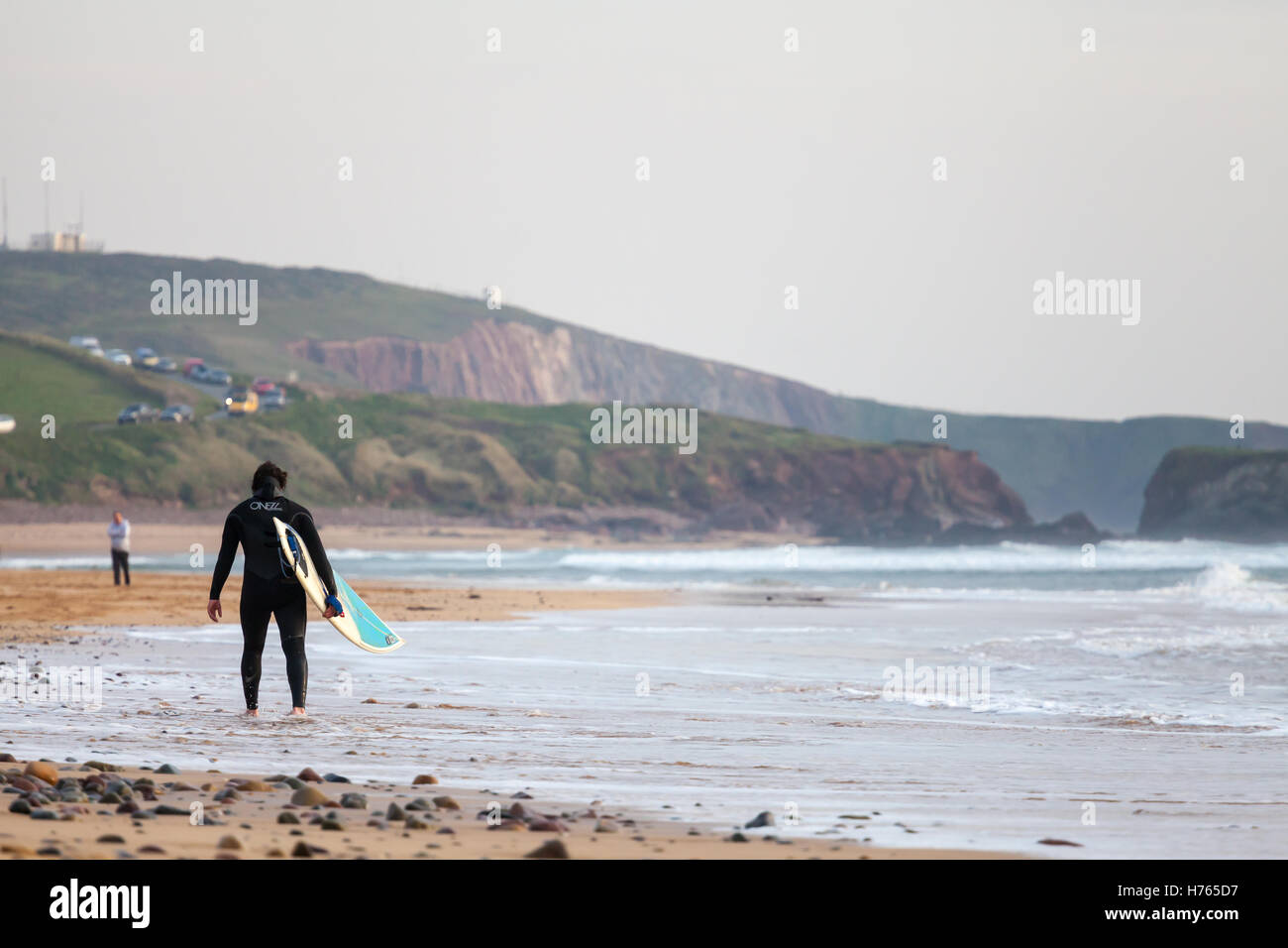 Surfer carrying a surfboard at Freshwater West Beach, Pembrokeshire in ...
