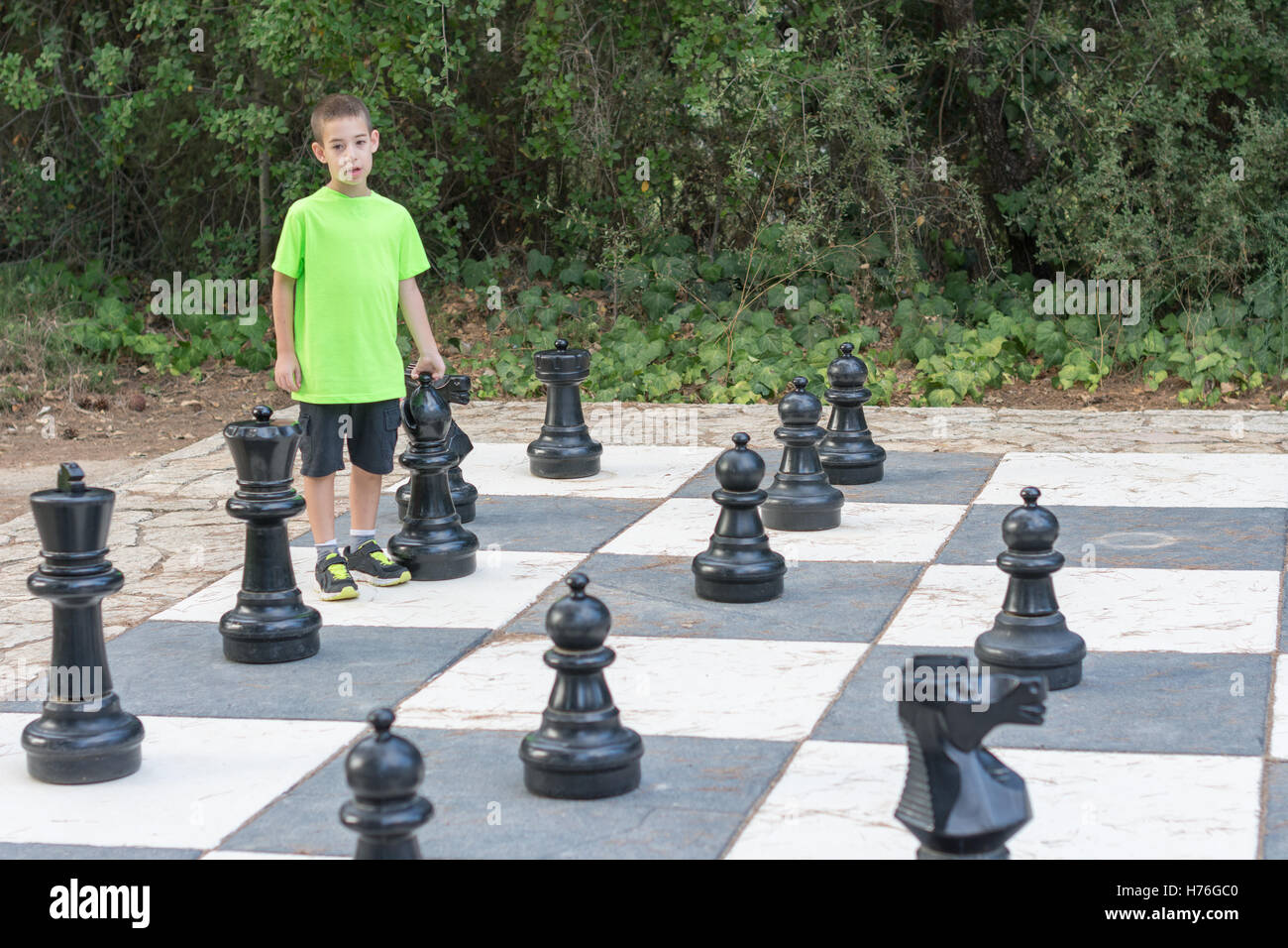 Boy playing a game of giant outdoor chess with big pieces in a green ...