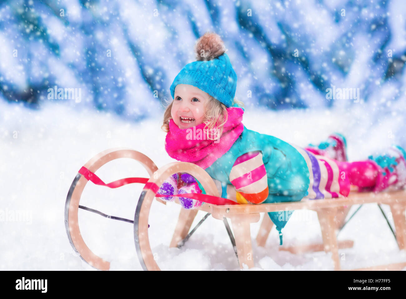 Little girl enjoying a sleigh ride. Child sledding. Toddler kid riding a sledge. Children play ...