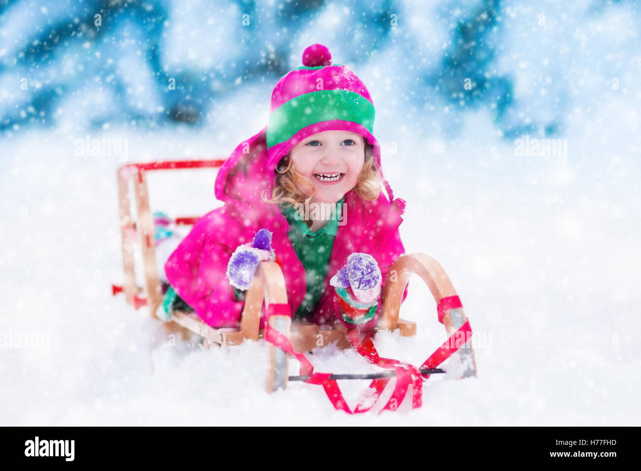 Little girl enjoying a sleigh ride. Child sledding. Toddler kid riding a sledge. Children play ...