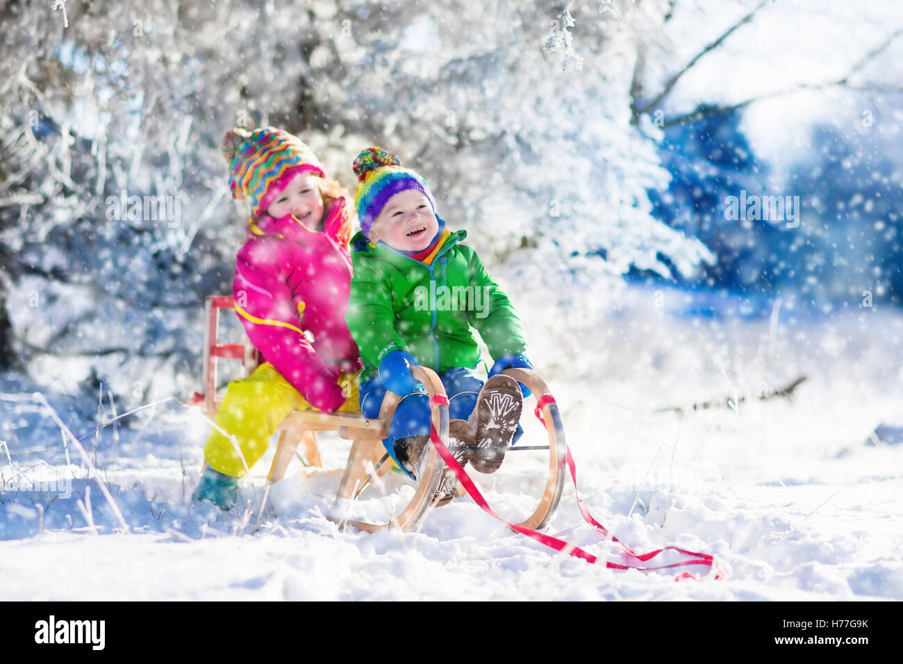 Little girl and boy enjoying sleigh ride. Child sledding. Toddler kid riding a sledge. Children ...