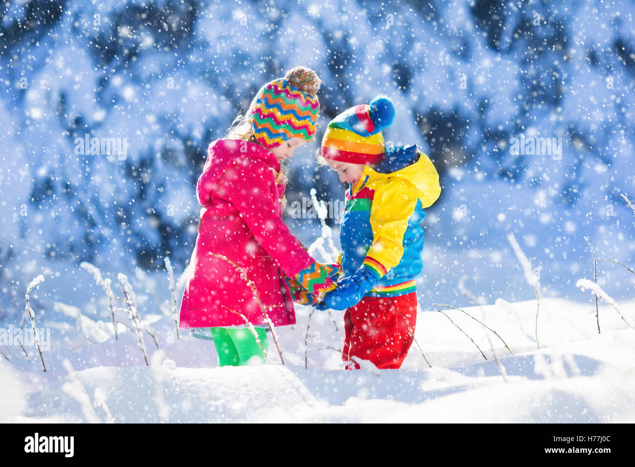Little girl and boy in red and green knitted hat catching snowflakes in ...