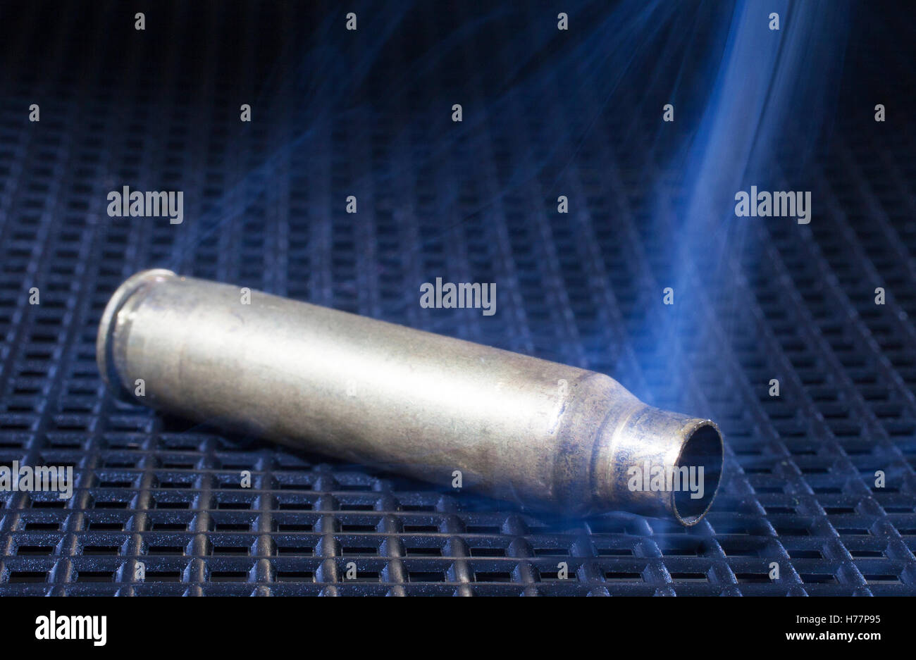 Empty rifle brass that is on a black grate with smoke around Stock ...