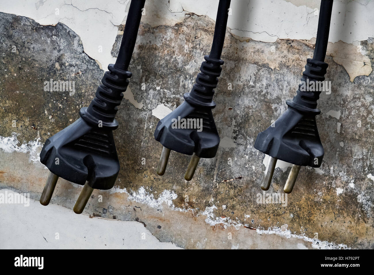 Closeup of three electrical plugs and damaged wall in the background ...