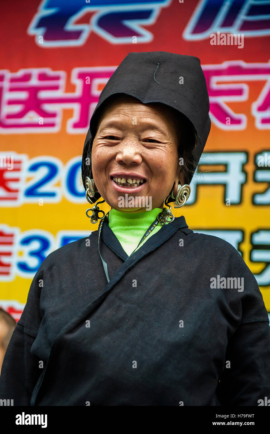 A Miao woman in traditional costume in front of a colored poster in ...