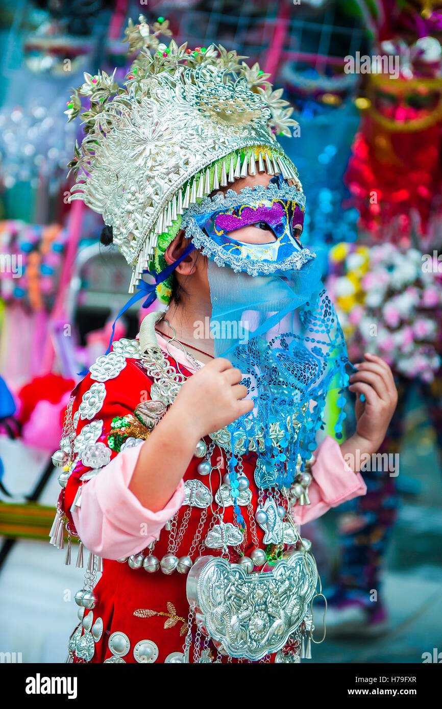 A Miao baby-girl in mask dressed in traditional costume along a ...