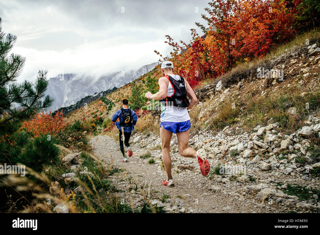 two athletes runners running from mountain along trail in autumn ...