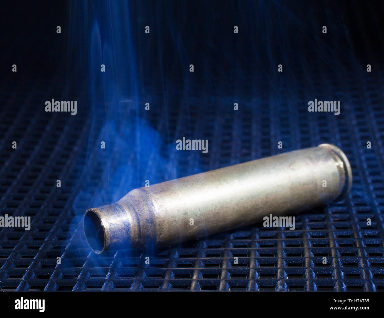Empty rifle casing on a black grate with smoke around Stock Photo - Alamy