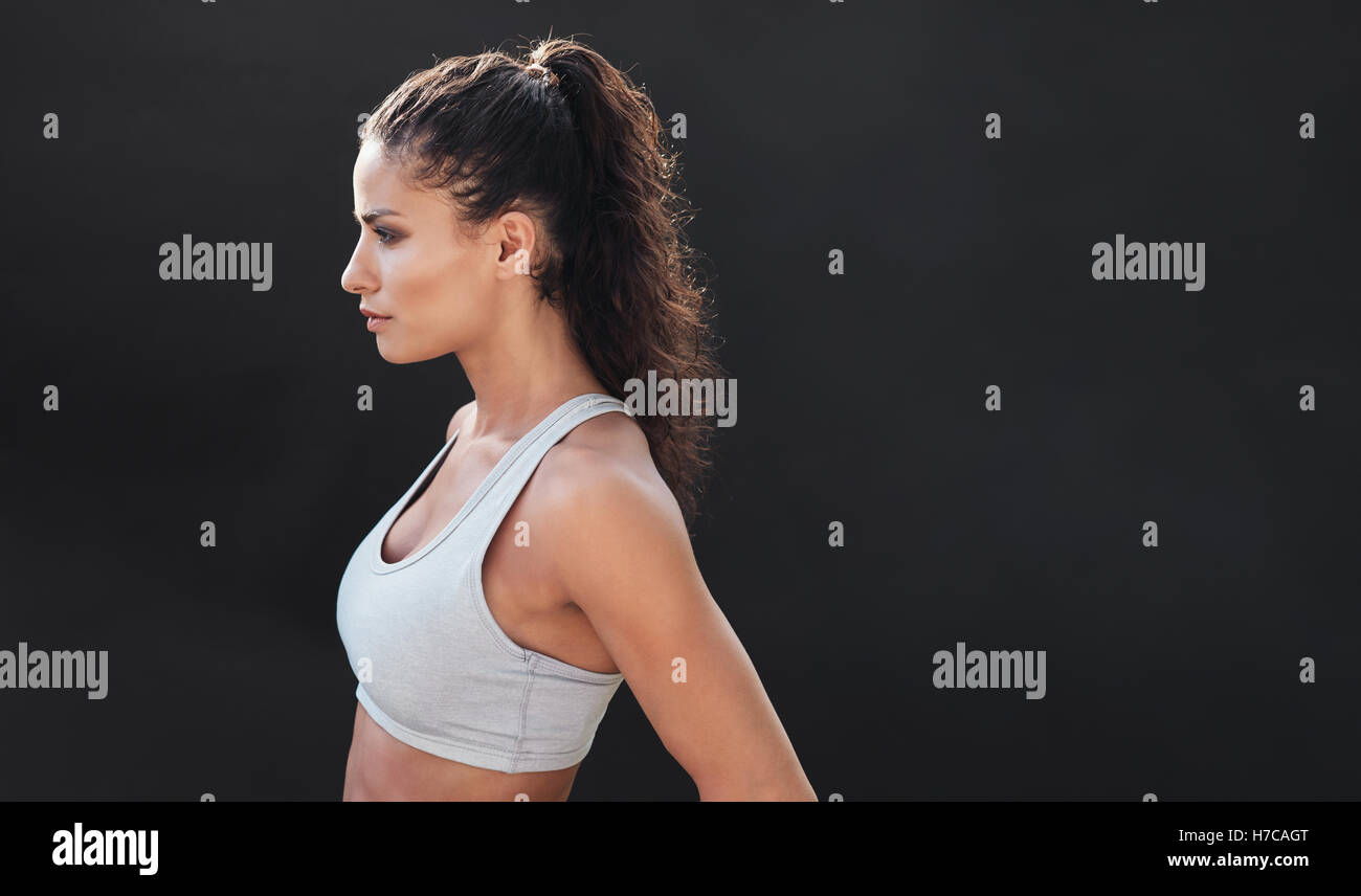 Side view of fit young woman in sports bra looking away on black ...