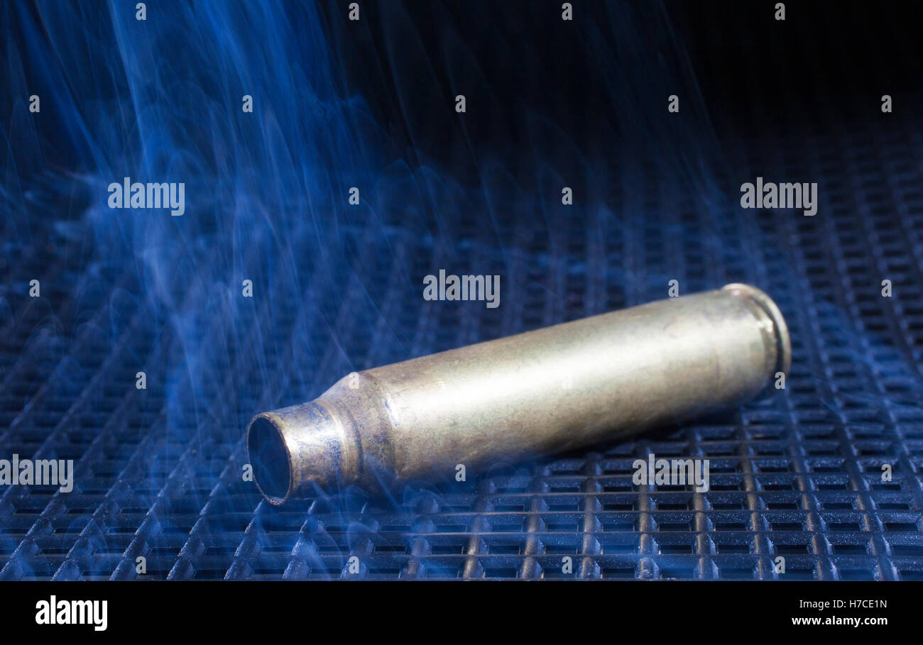 Empty rifle casing on a black grate surrounded by smoke Stock Photo - Alamy