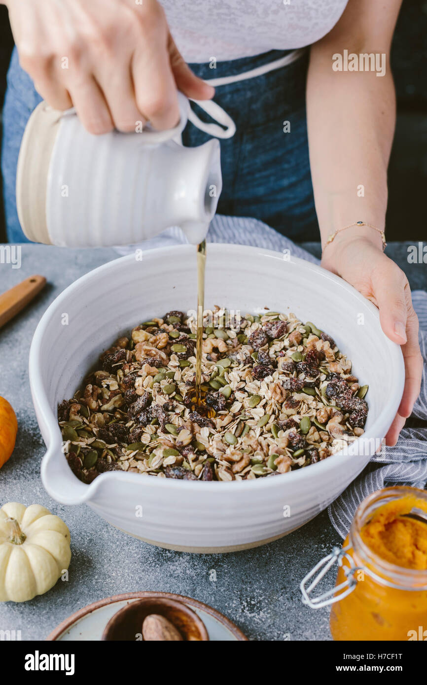 A woman is pouring maple syrup into a nut mixture to make pumpkin ...