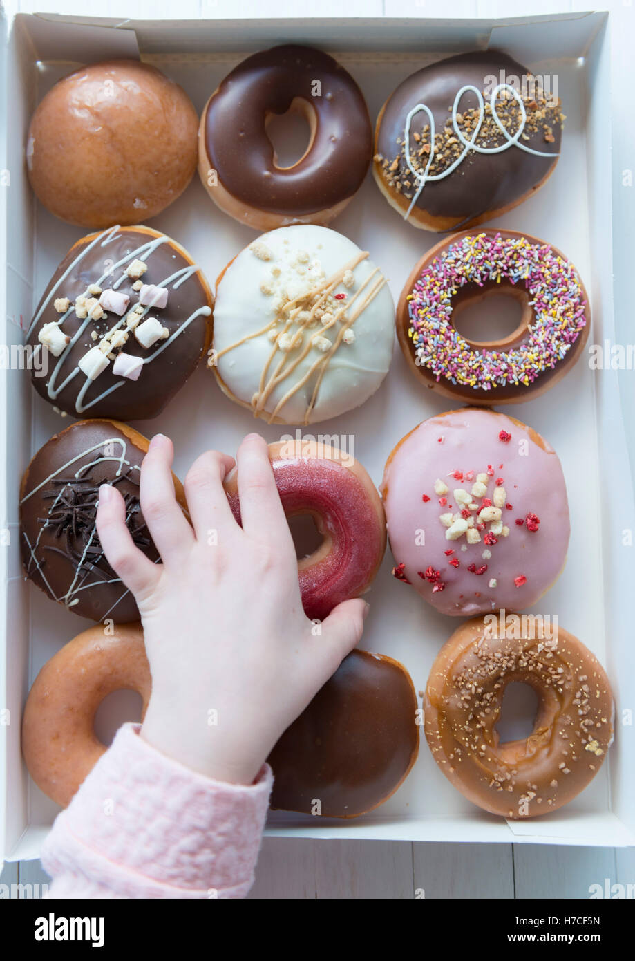 A hand selecting a donut from a box of a dozen donuts Stock Photo - Alamy