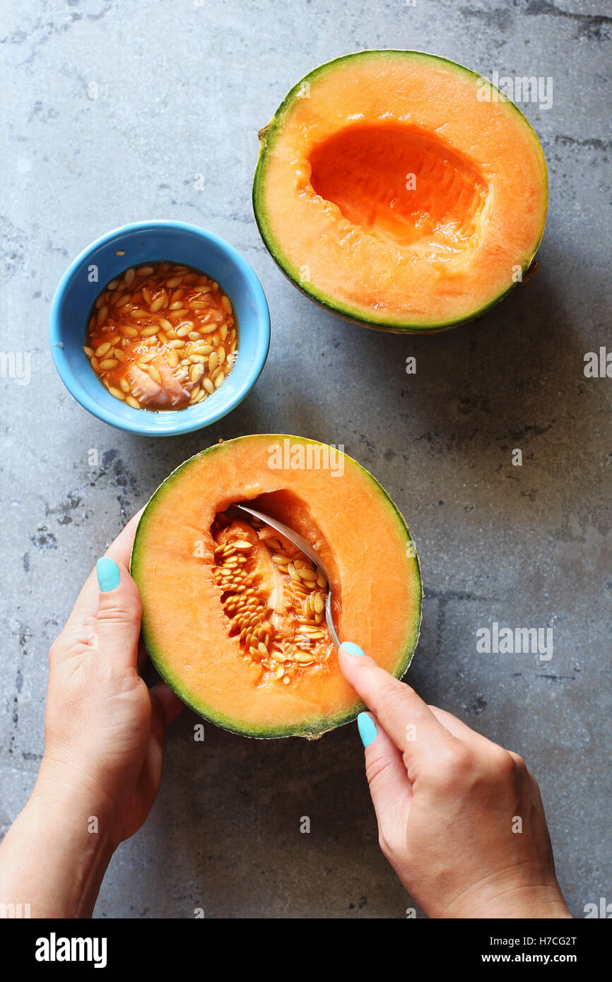 Female hand scooping out the seeds from a cantaloupe.Top view Stock ...