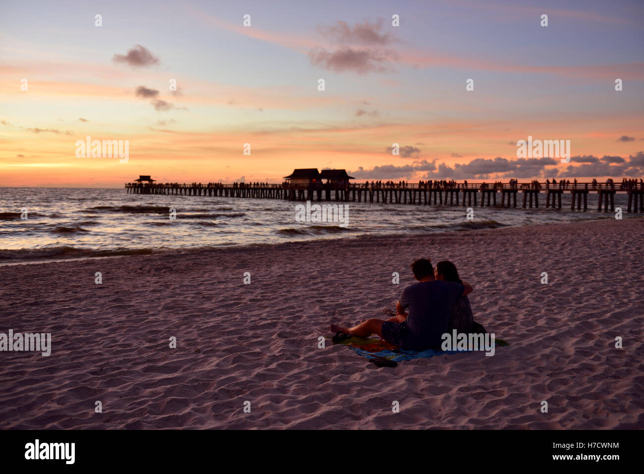 Couple on sandy beach in near silhouette with Naples, Florida pier ...